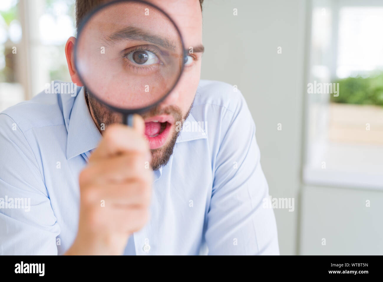 Handsome business man holding magnifying glass close to face, big eyes ...
