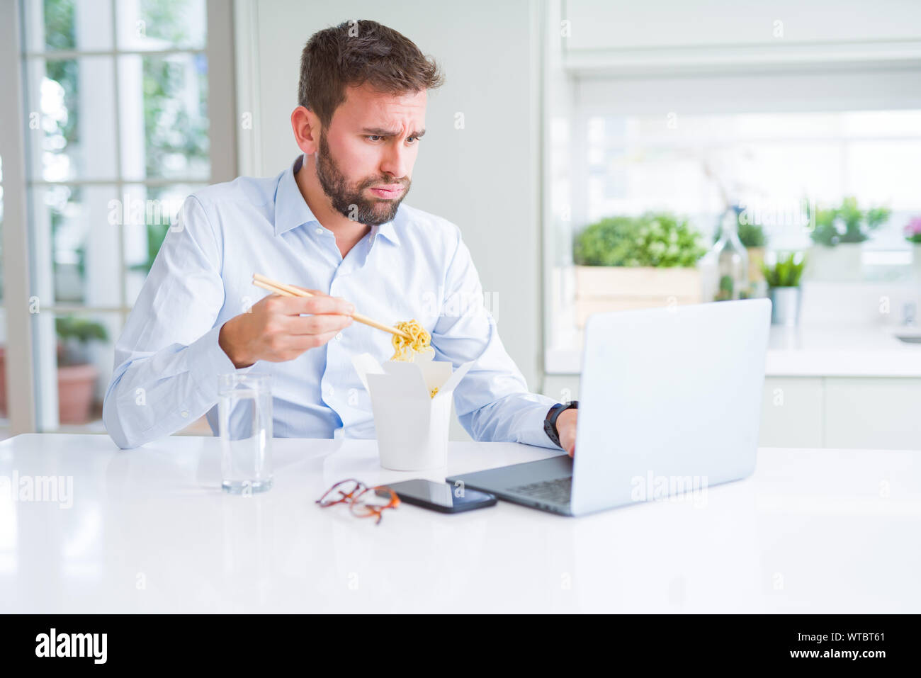 Business man eating take away asian noodles food while working using ...