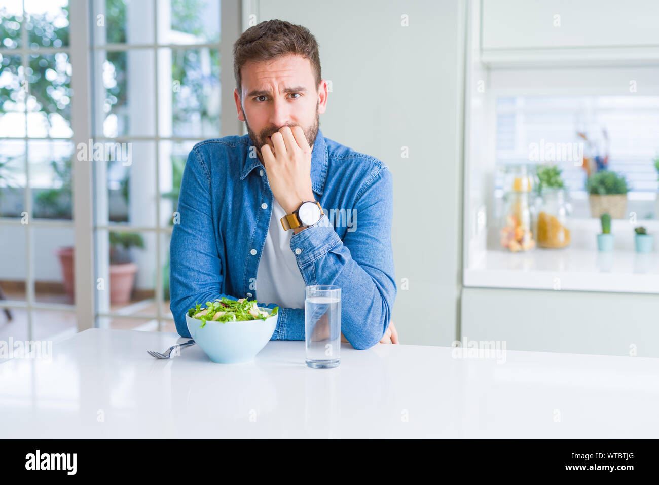 Handsome man eating fresh healthy salad looking stressed and nervous ...