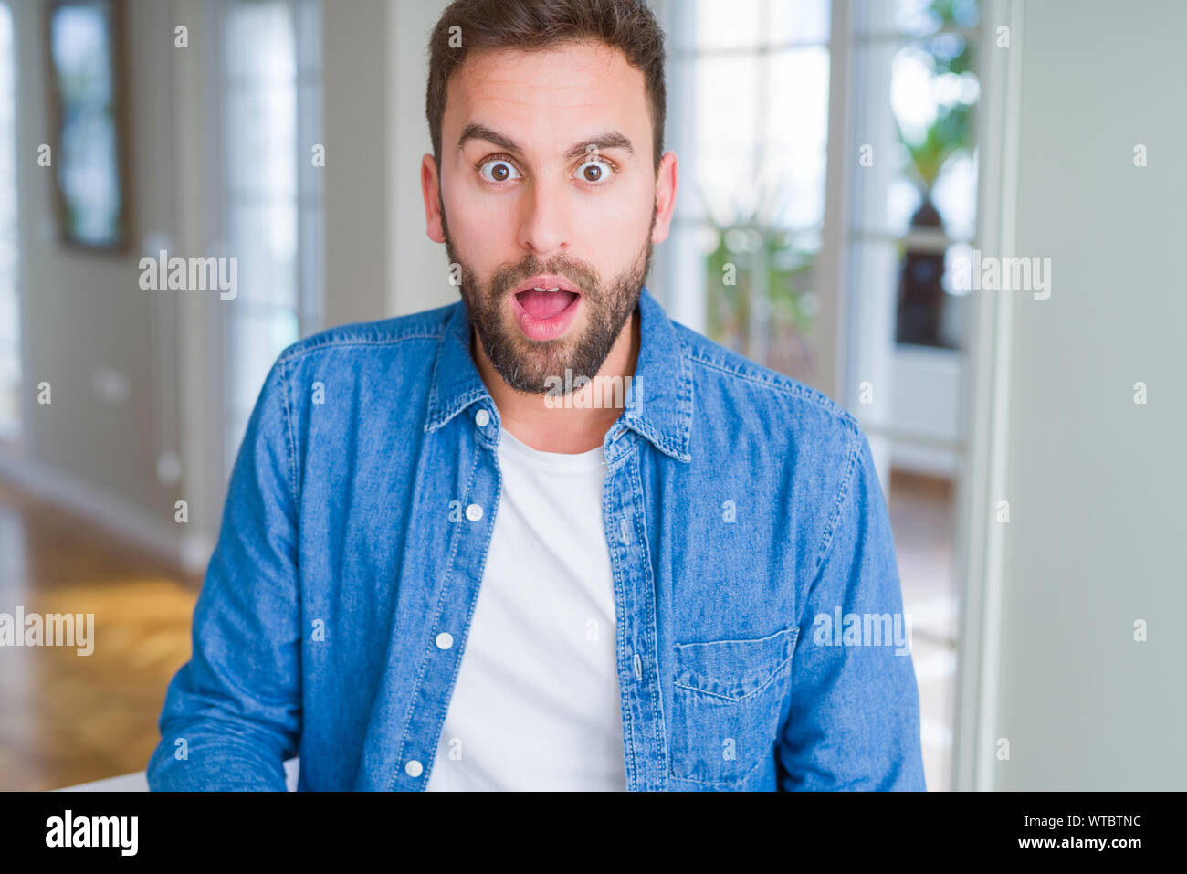 Handsome man at home afraid and shocked with surprise expression, fear ...