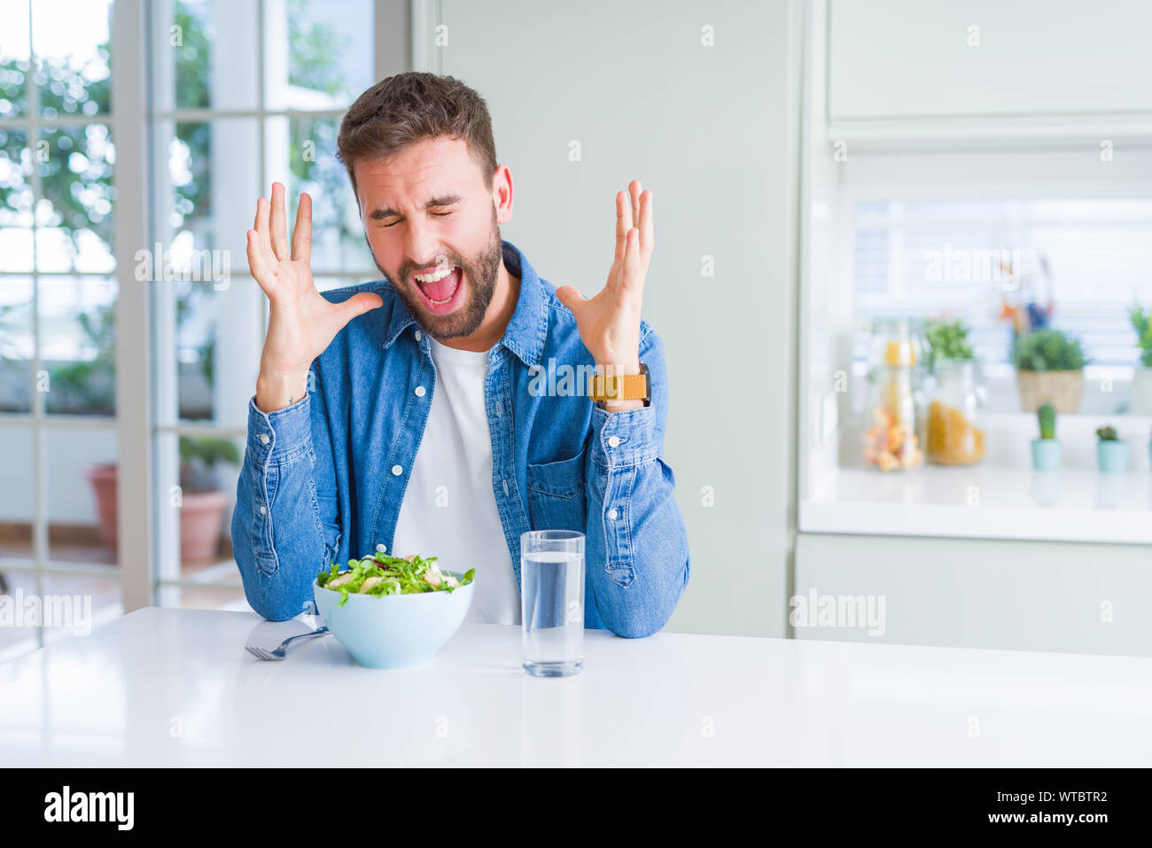 Handsome man eating fresh healthy salad celebrating mad and crazy for ...