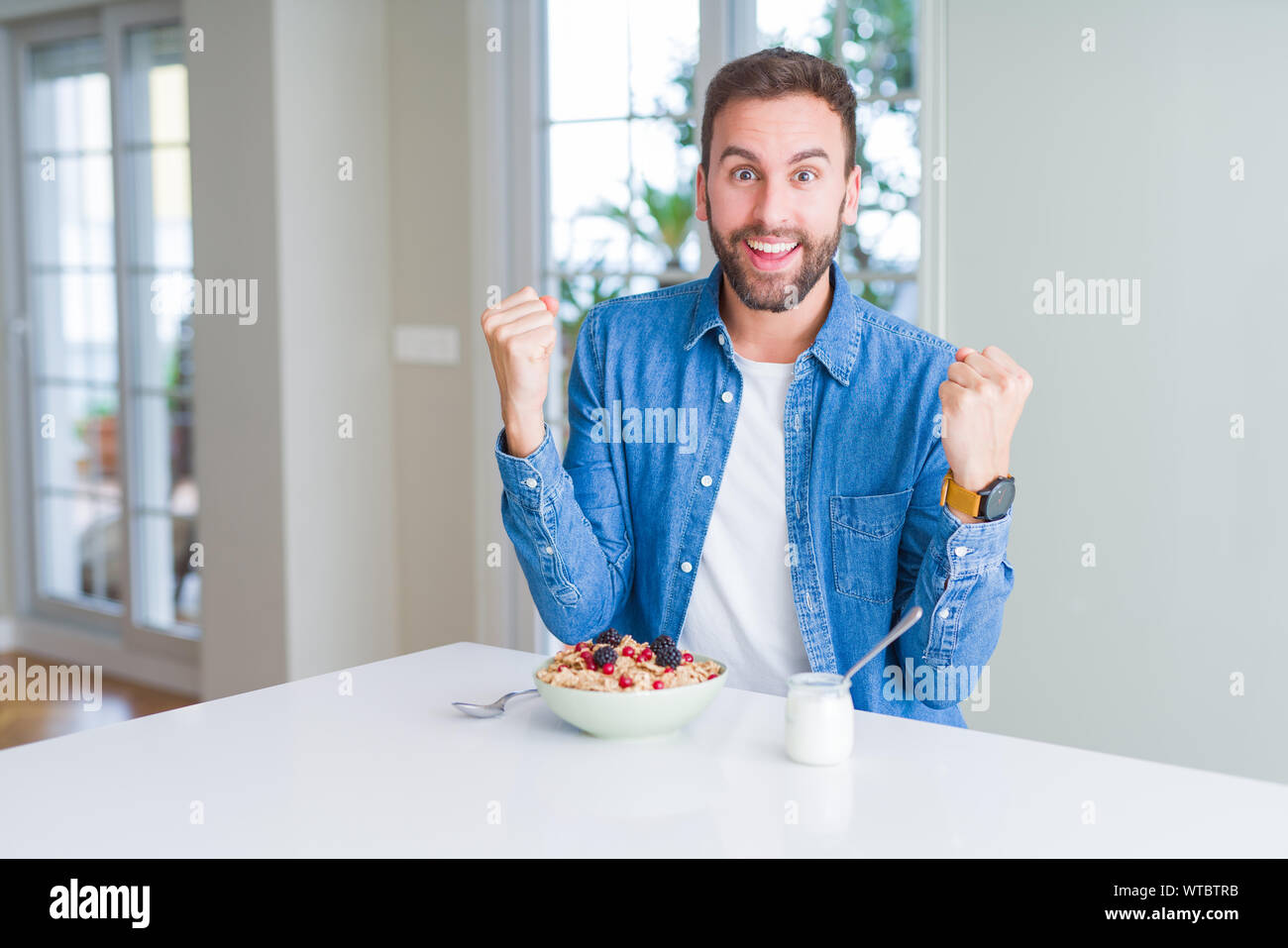 Handsome man eating cereals for breakfast at home celebrating surprised ...