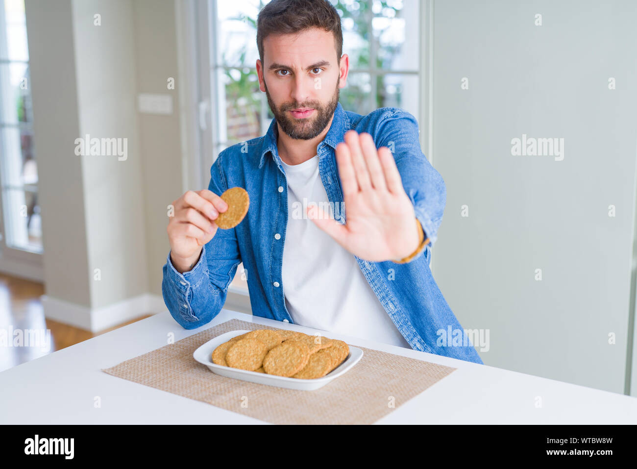 Handsome man eating healthy whole grain biscuit with open hand doing ...
