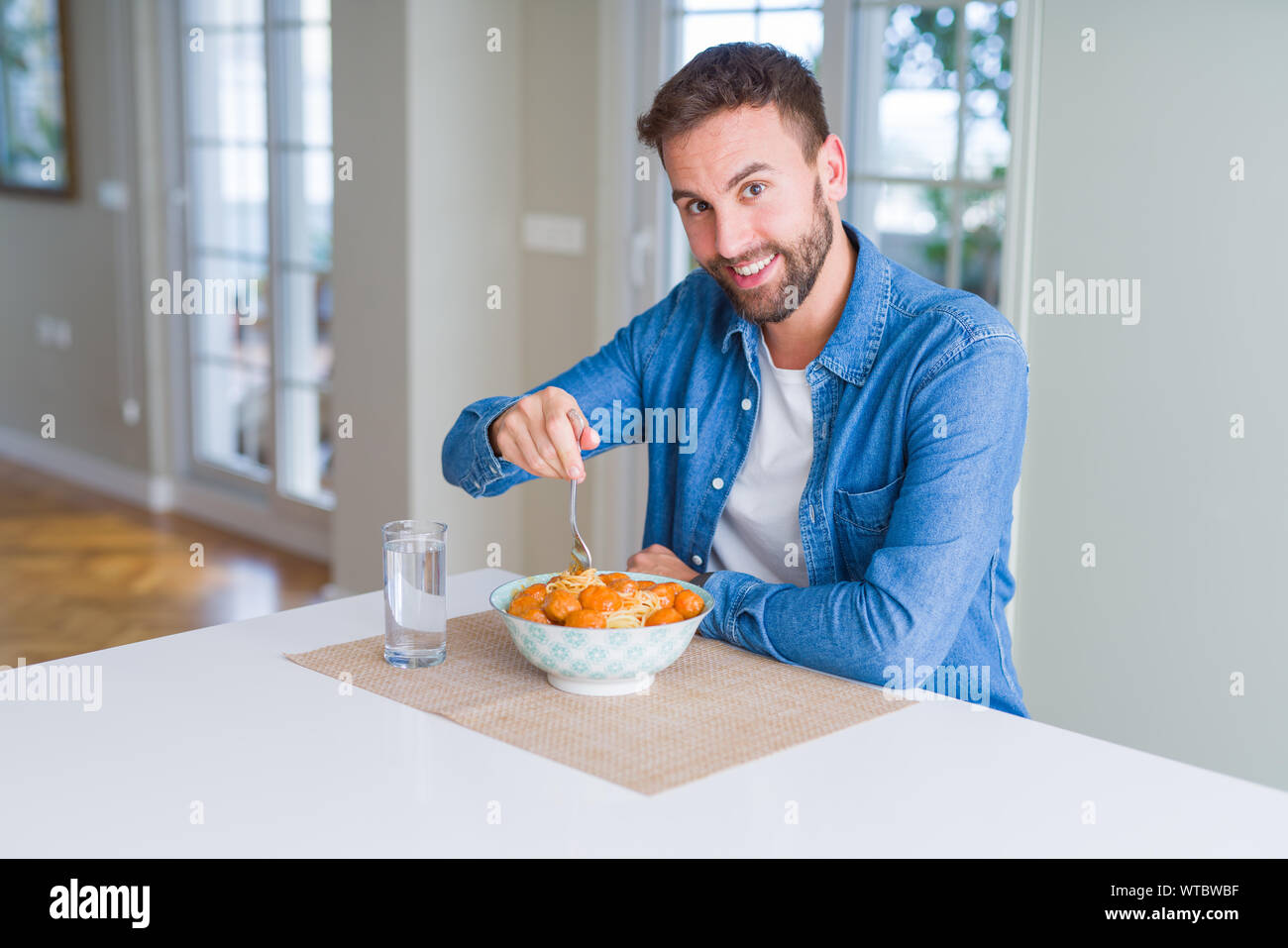 Handsome man eating pasta with meatballs and tomato sauce at home while ...