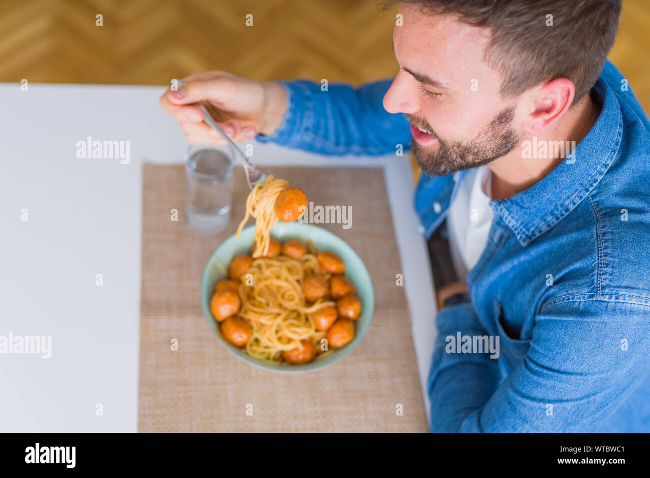 Handsome man eating pasta with meatballs and tomato sauce at home while ...