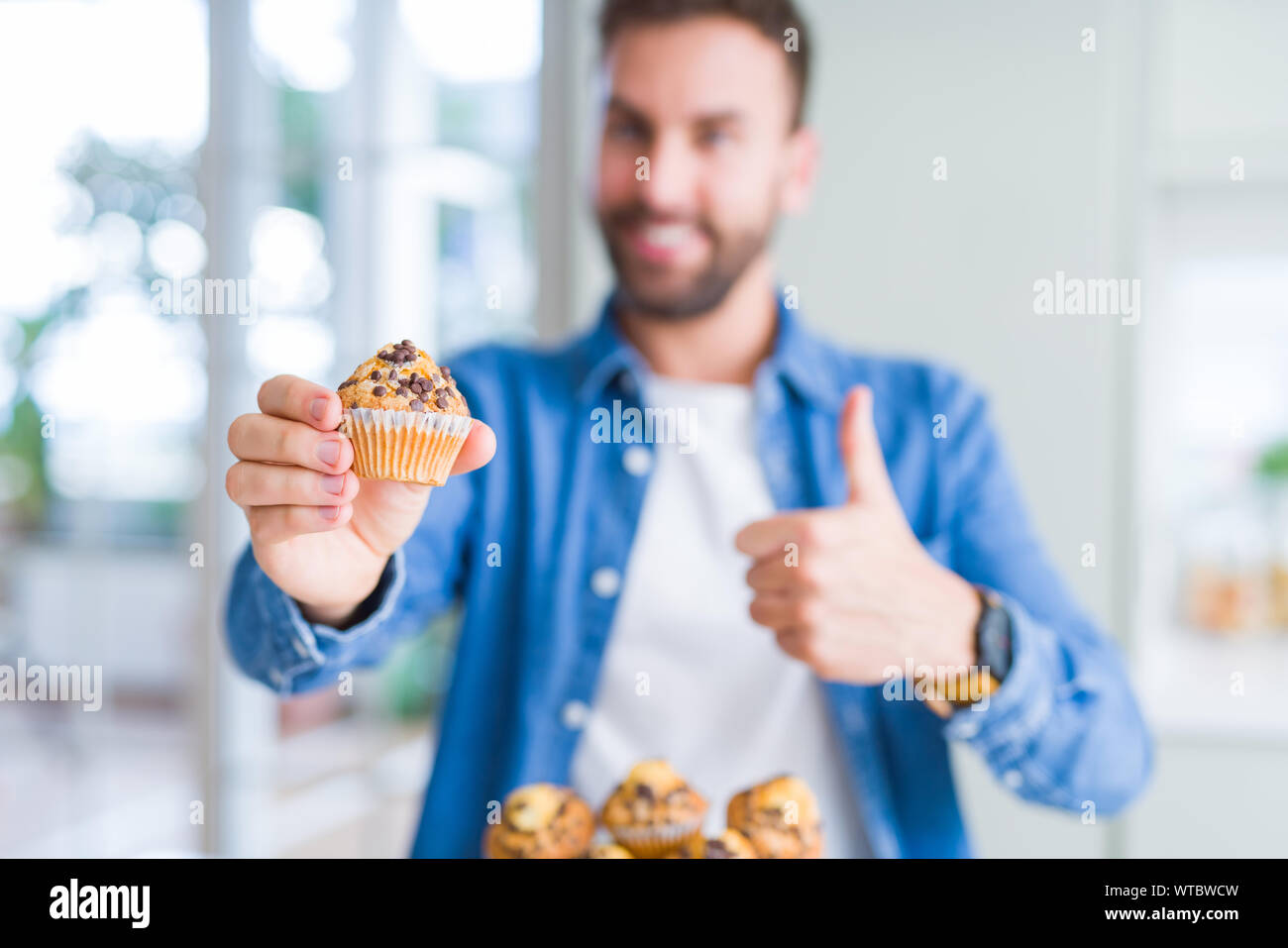 Handsome man eating chocolate chips muffin happy with big smile doing ...