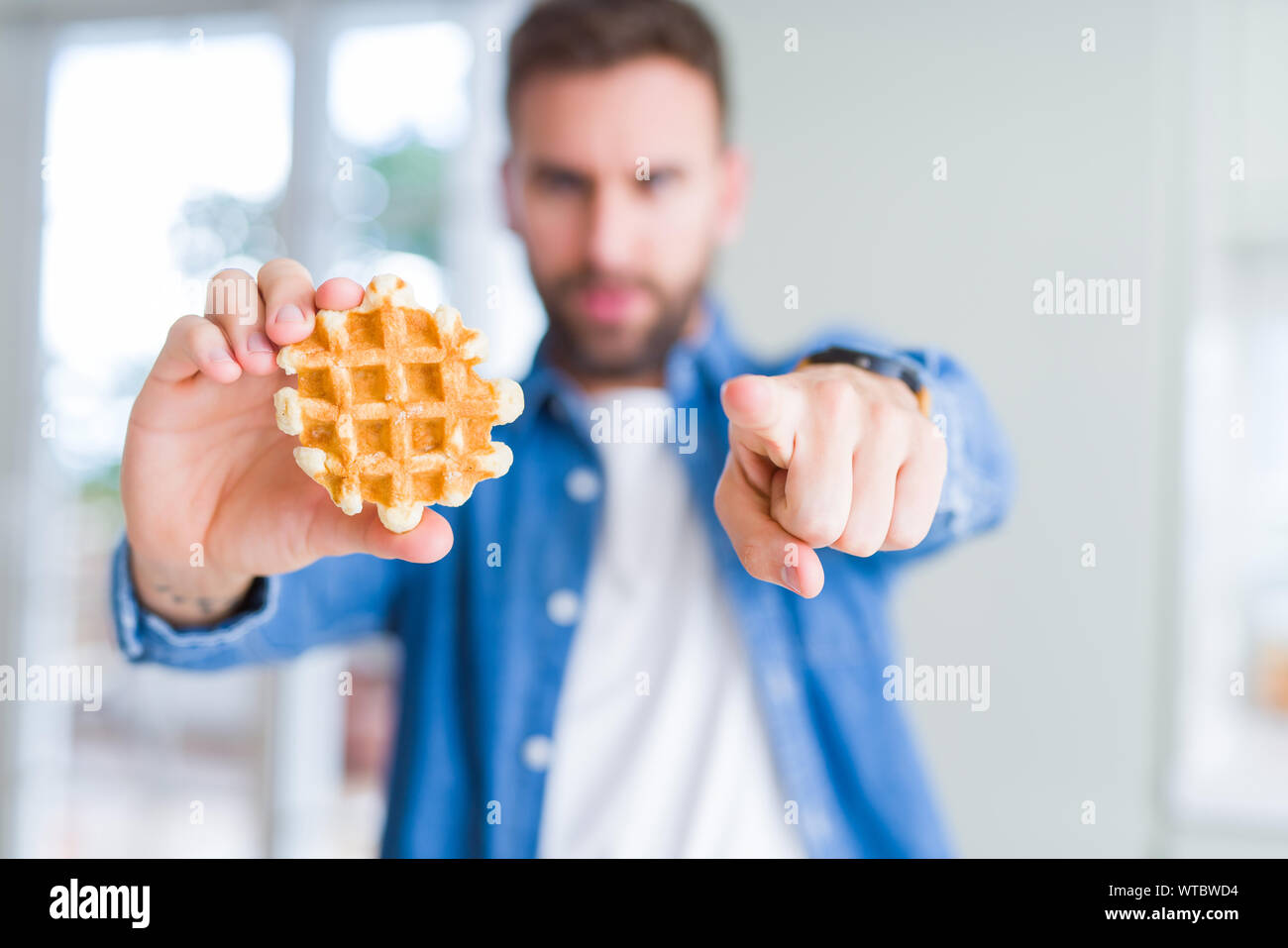 Handsome man eating sweet Belgian pancakes pointing with finger to the ...