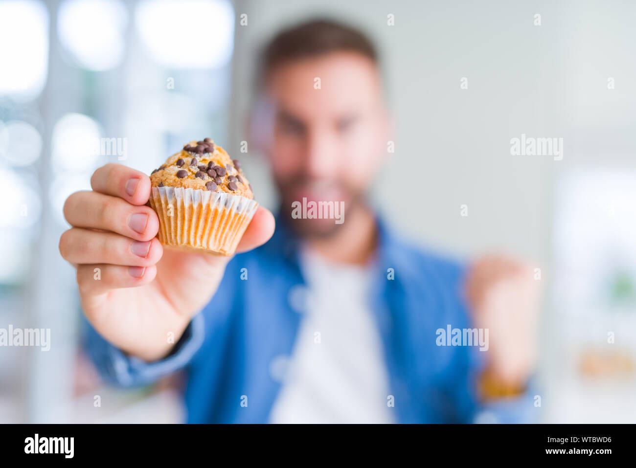 Handsome man eating chocolate chips muffin screaming proud and ...