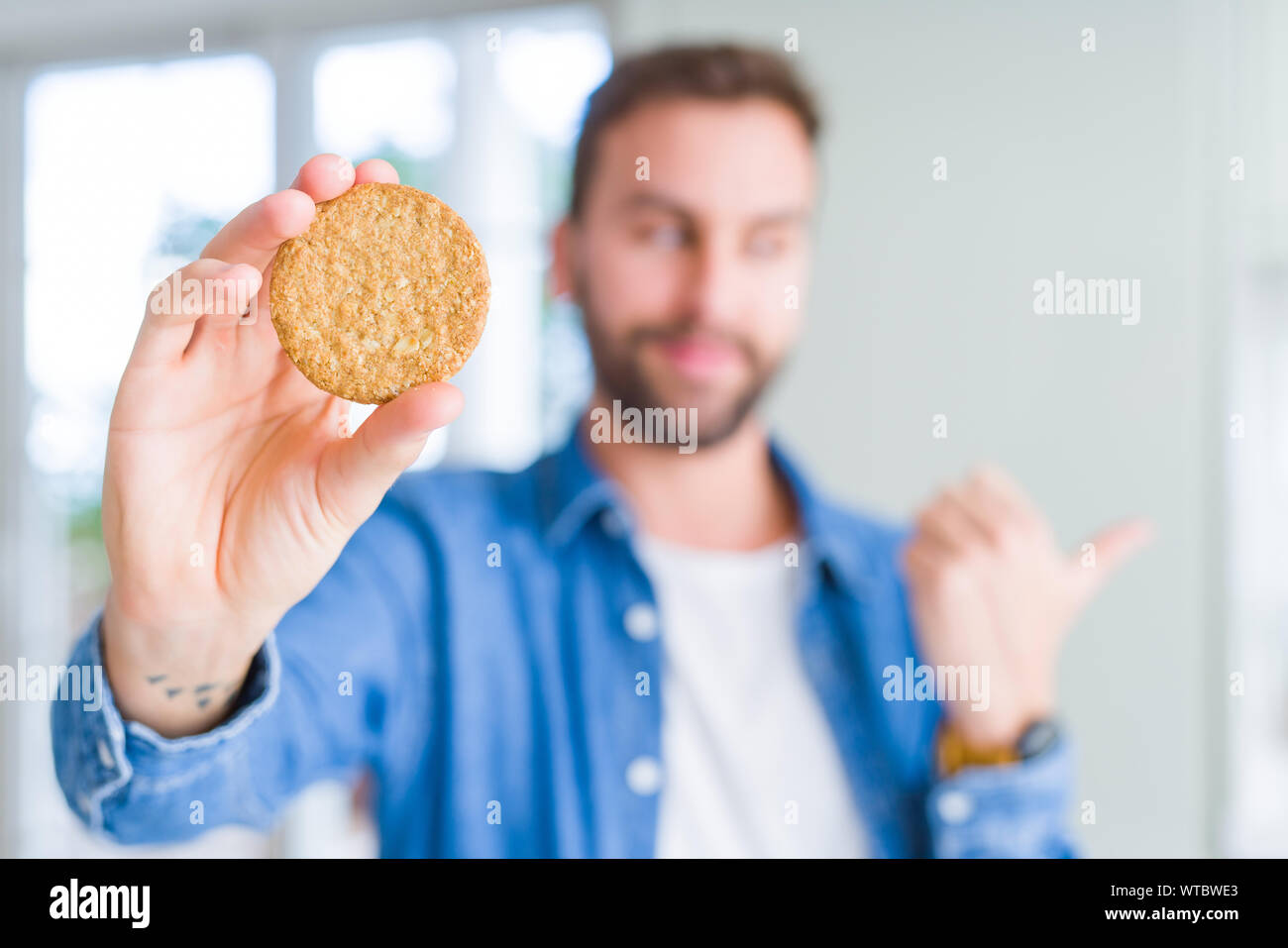 Handsome man eating healthy whole grain biscuit pointing and showing ...