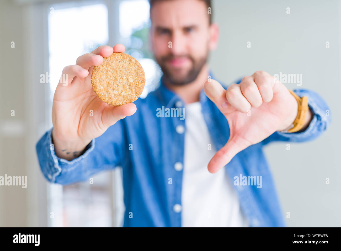 Handsome man eating healthy whole grain biscuit with angry face ...