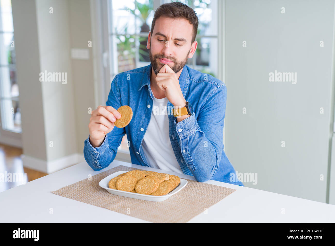 Handsome man eating healthy whole grain biscuit serious face thinking ...