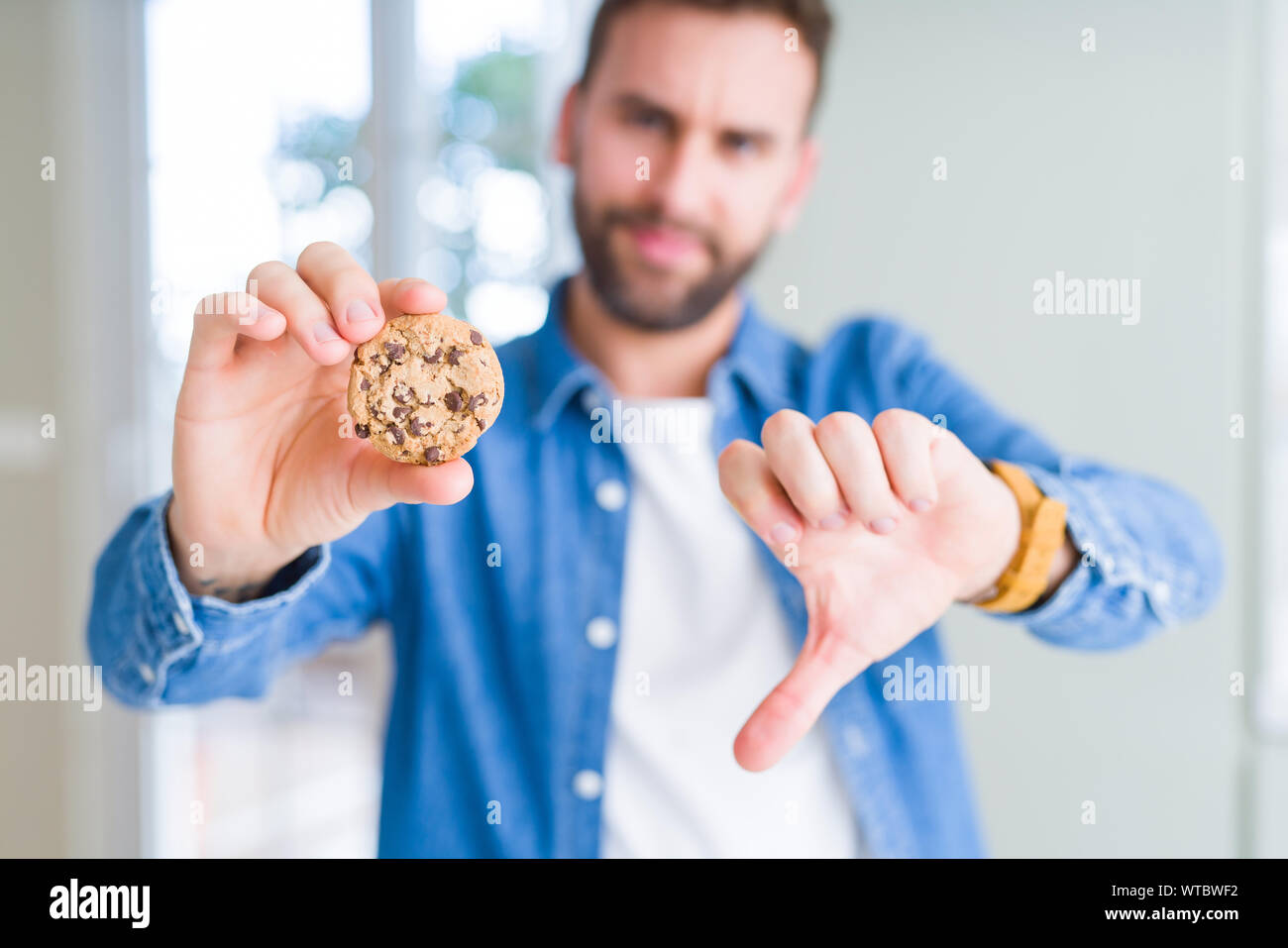 Handsome man eating chocolate chips cookies with angry face, negative ...