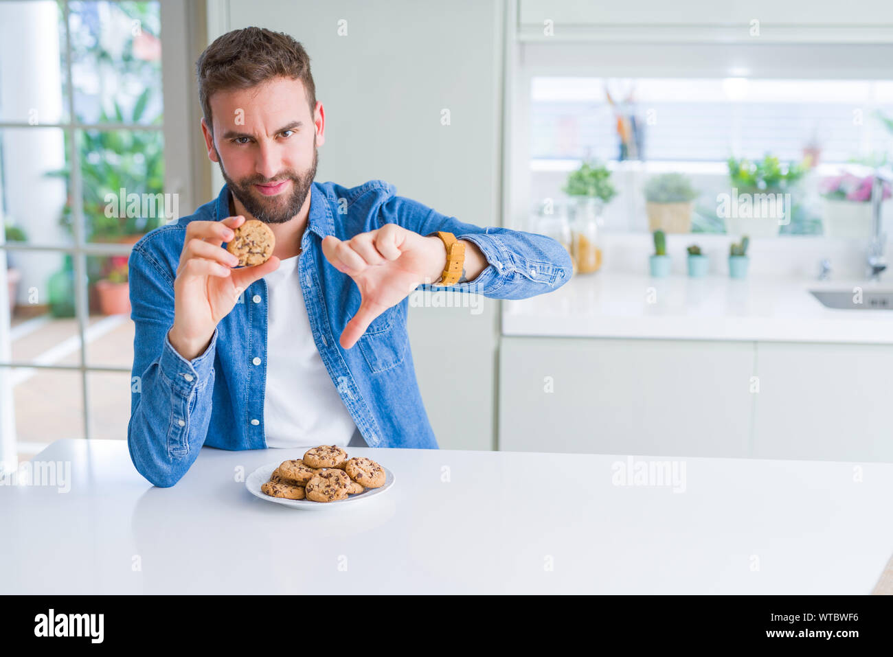 Handsome man eating chocolate chips cookies with angry face, negative ...