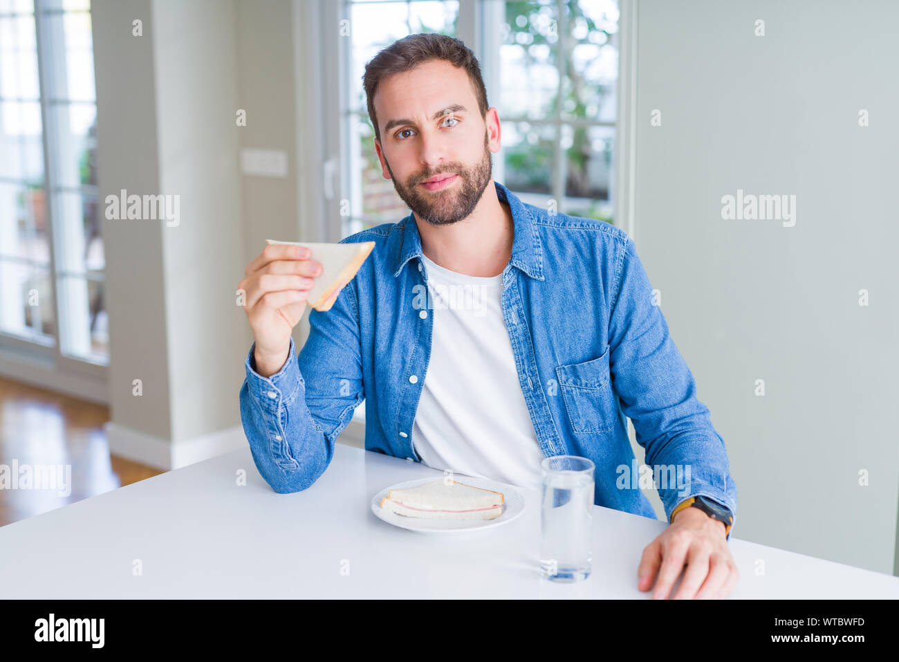 Handsome man eating healthy sandwich with a confident expression on ...