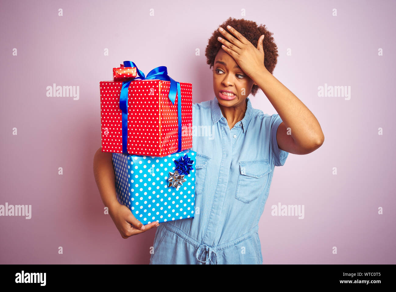 African american woman holding birthday gifts over pink isolated ...