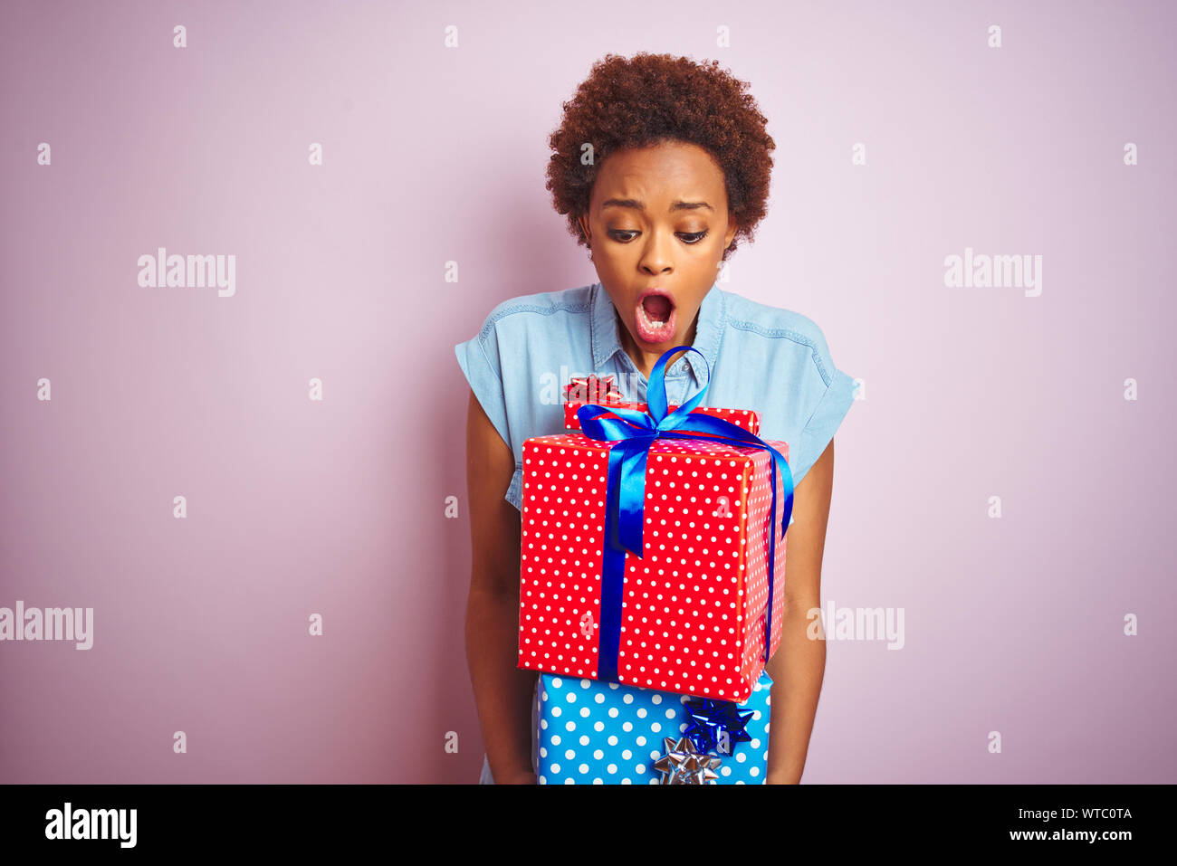 African american woman holding birthday gifts over pink isolated ...
