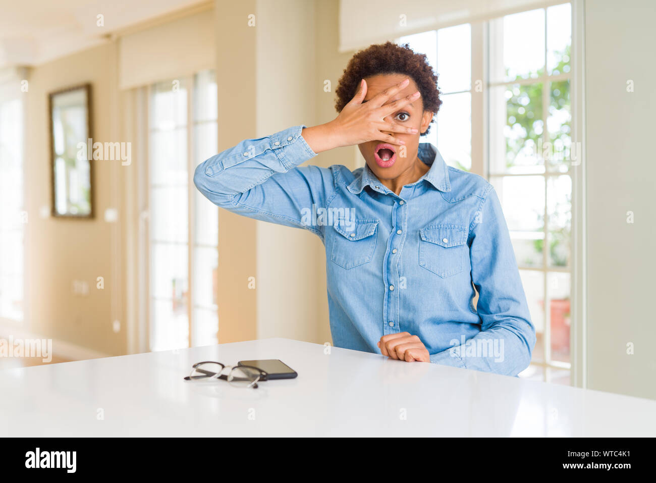 Young beautiful african american woman peeking in shock covering face ...