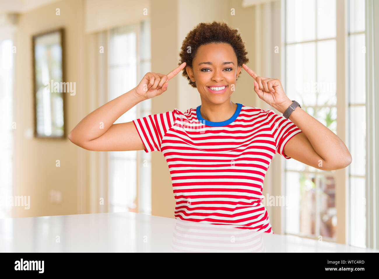 Young beautiful african american woman at home Smiling pointing to head ...