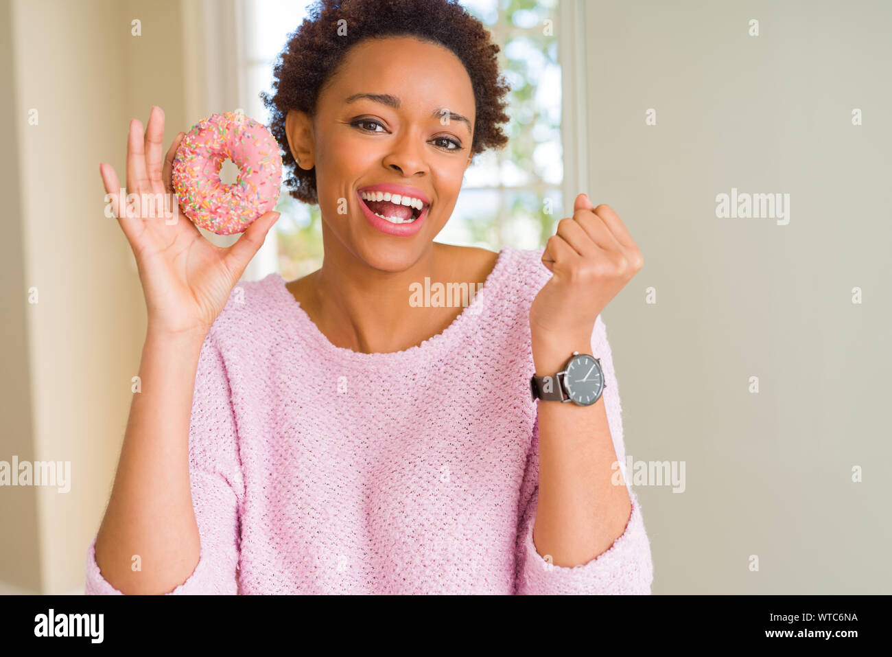 Young african american woman eating pink sugar donut screaming proud ...