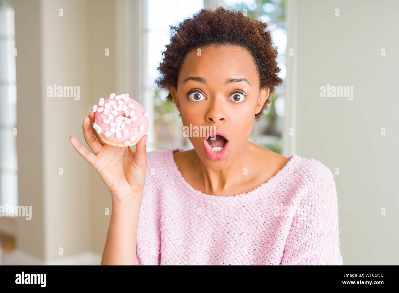 Young african american woman eating pink sugar marshmallows donut ...