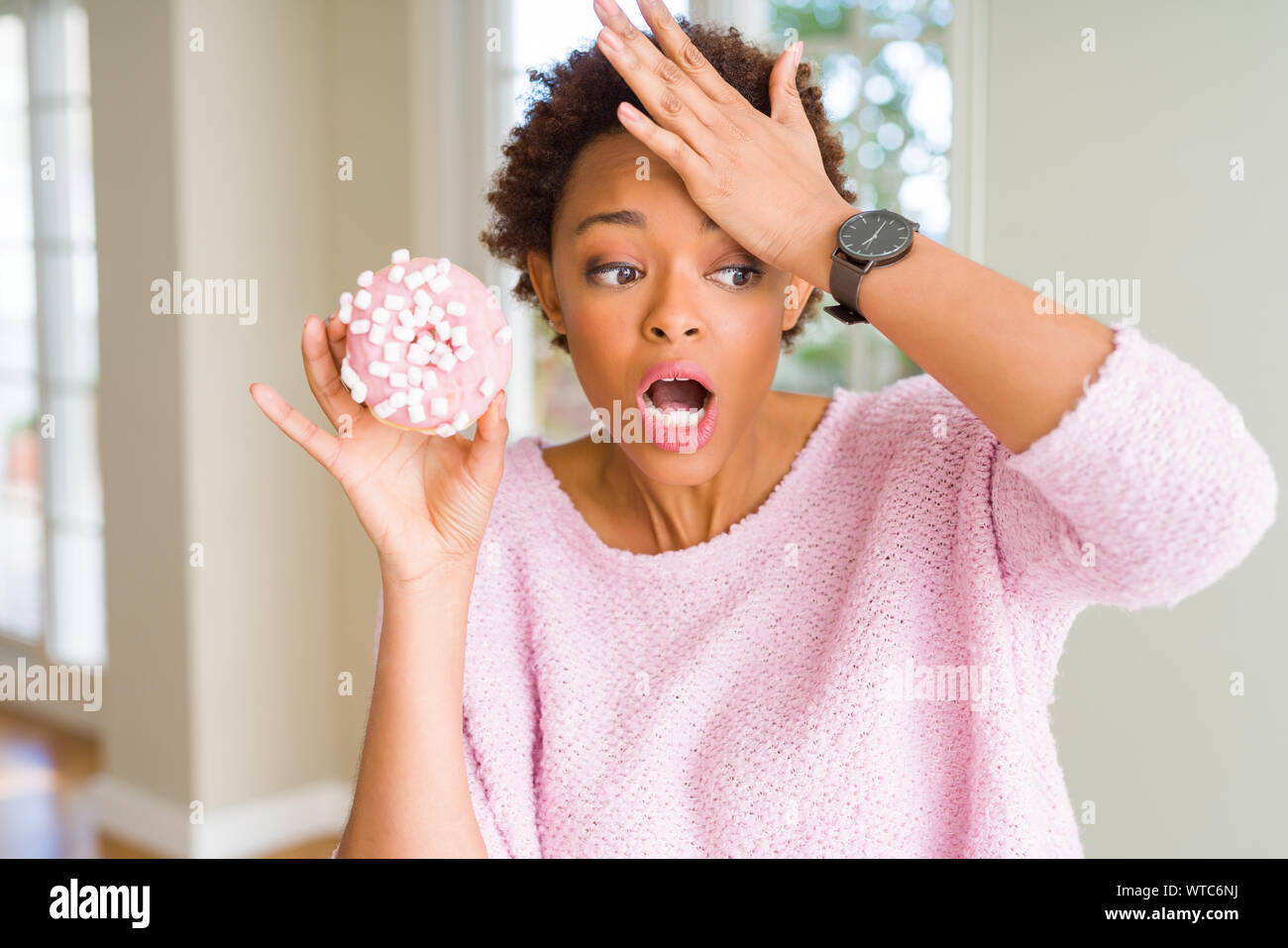 Young african american woman eating pink sugar marshmallows donut ...