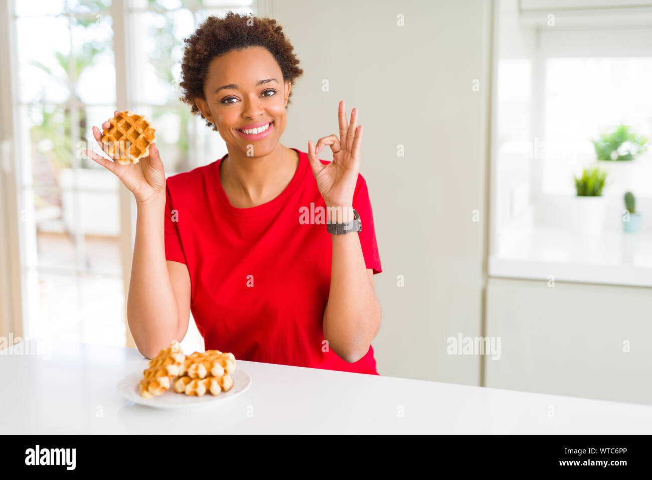 Young african american woman eating sweet waffle doing ok sign with ...