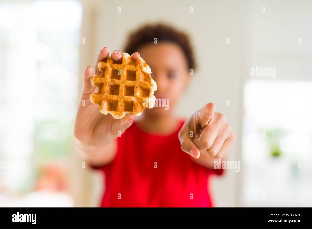 Young african american woman eating sweet waffle pointing with finger ...