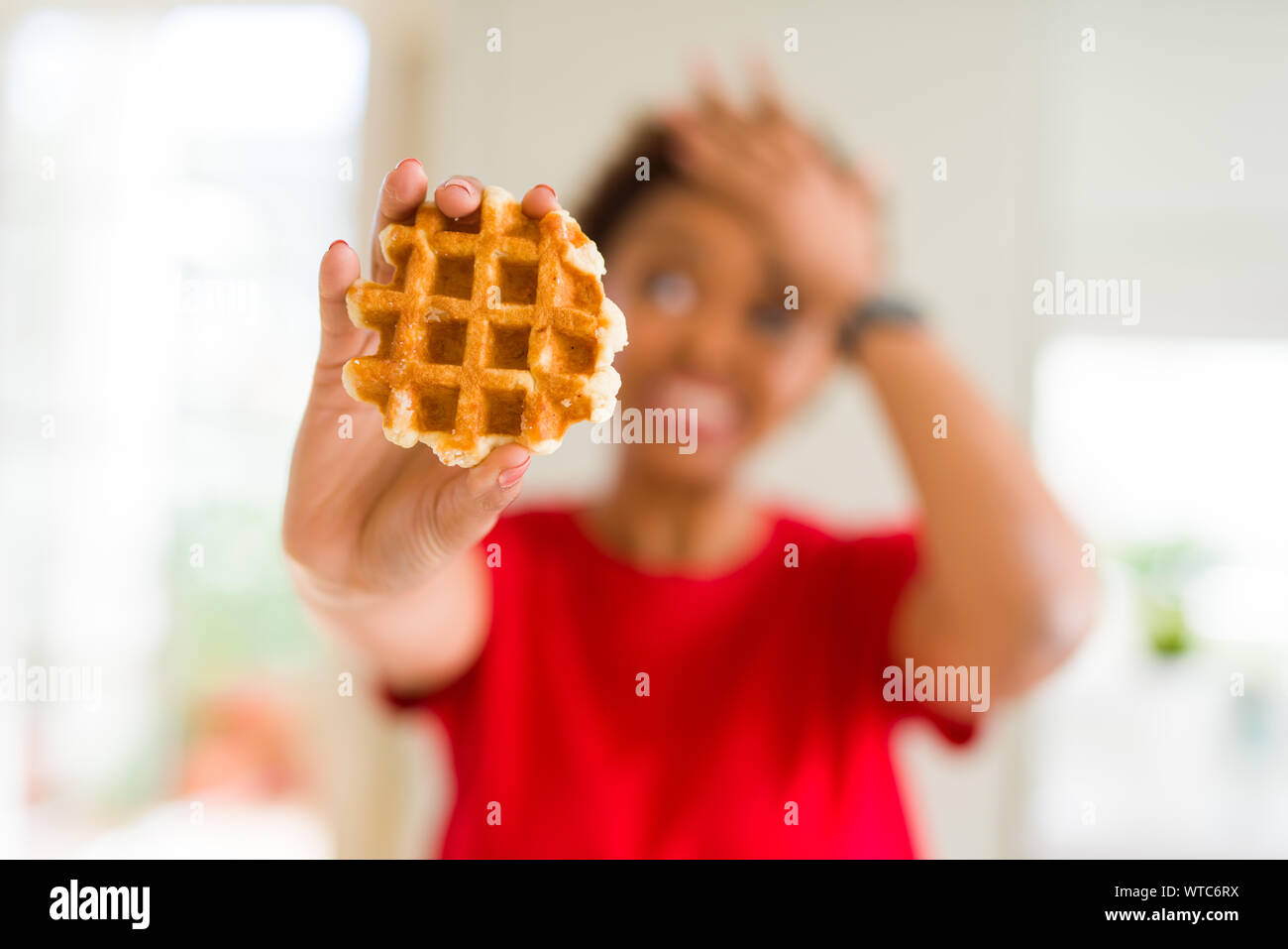 Young african american woman eating sweet waffle stressed with hand on ...