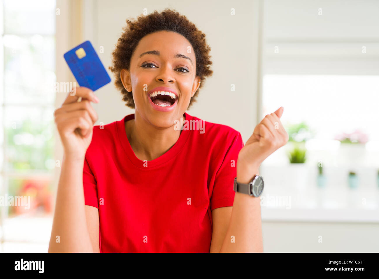 Young african american woman holding credit card screaming proud and ...