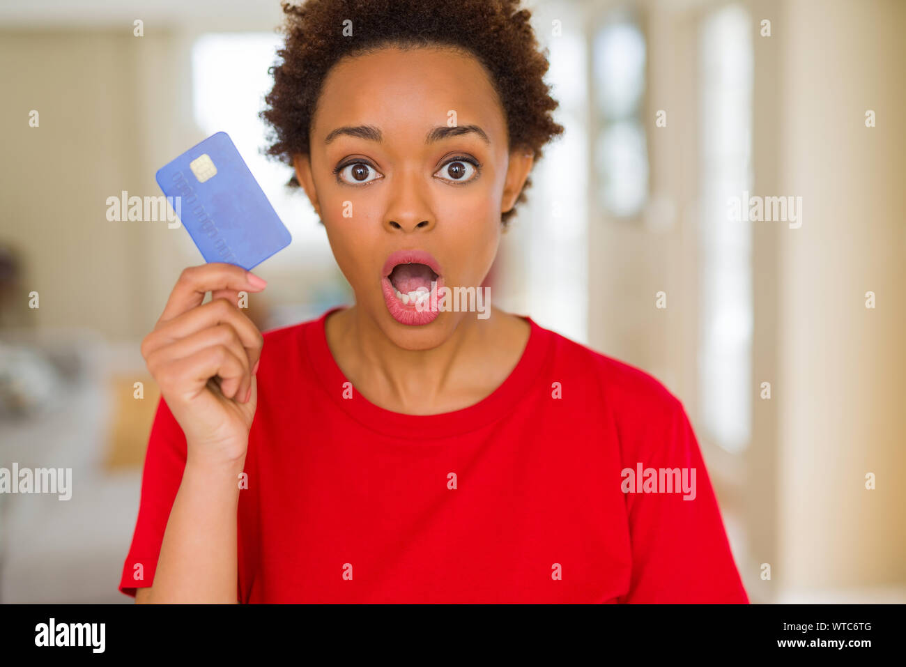 Young african american woman holding credit card scared in shock with a ...
