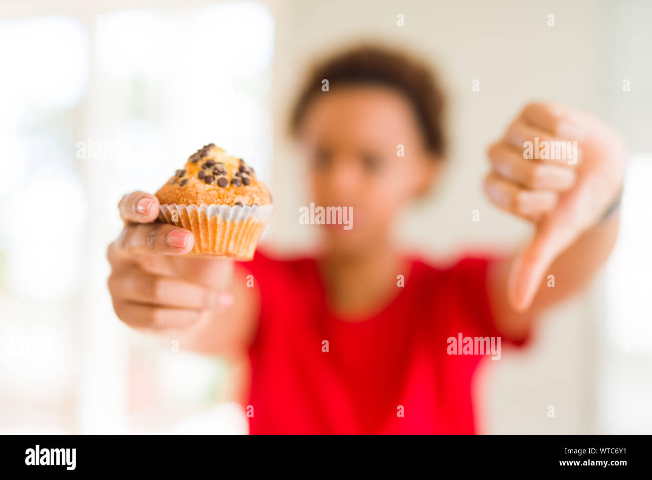 Young african american woman eating chocolate chips muffins with angry ...