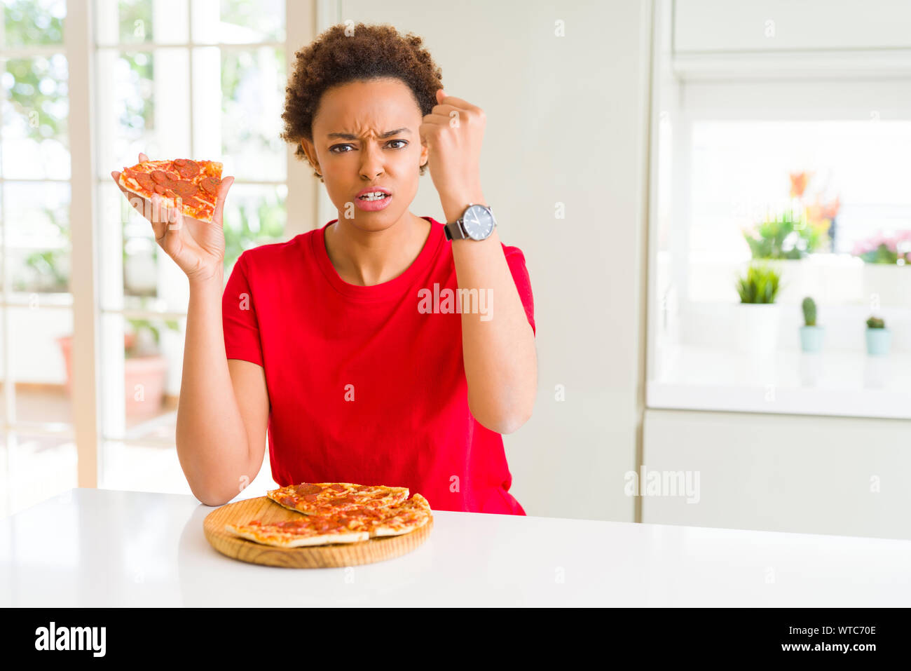 Young african american woman eating tasty peperoni pizza annoyed and ...