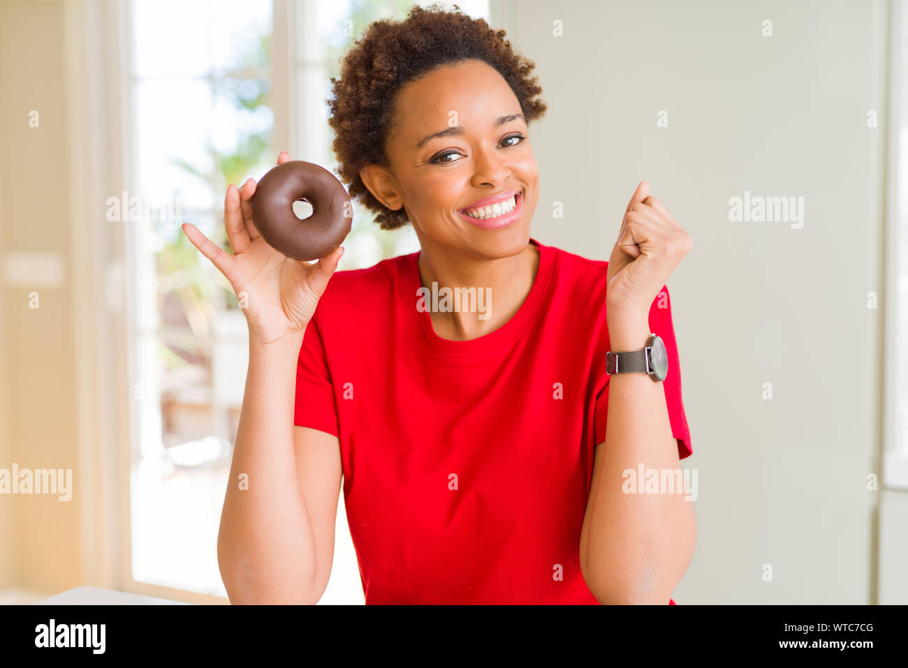 Young african american woman eating chocolate donut screaming proud and ...