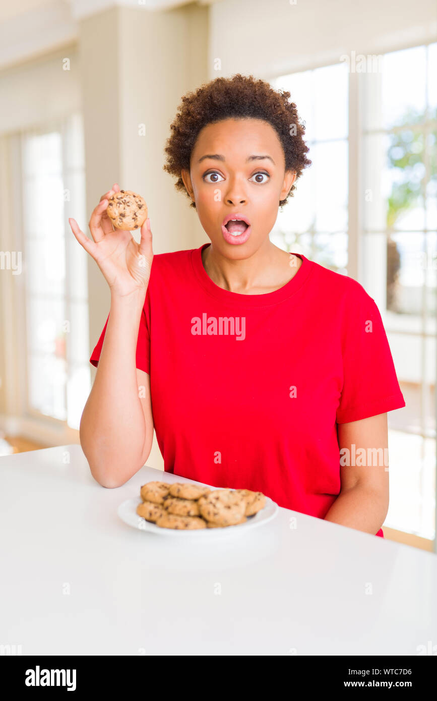 Young african american woman eating chocolate chips cookies scared in ...