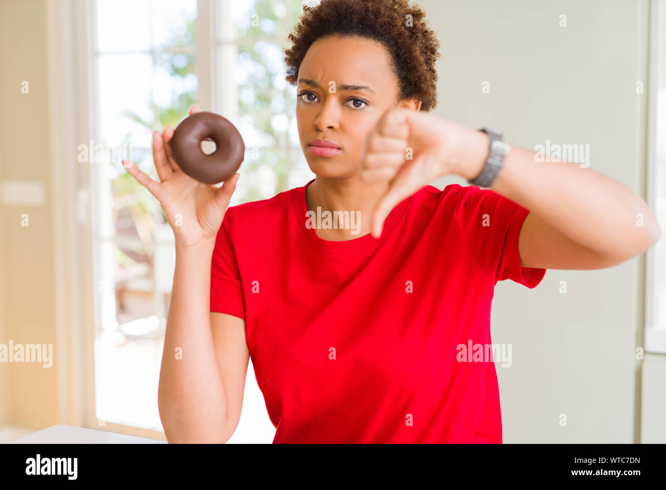 Young african american woman eating chocolate donut with angry face ...