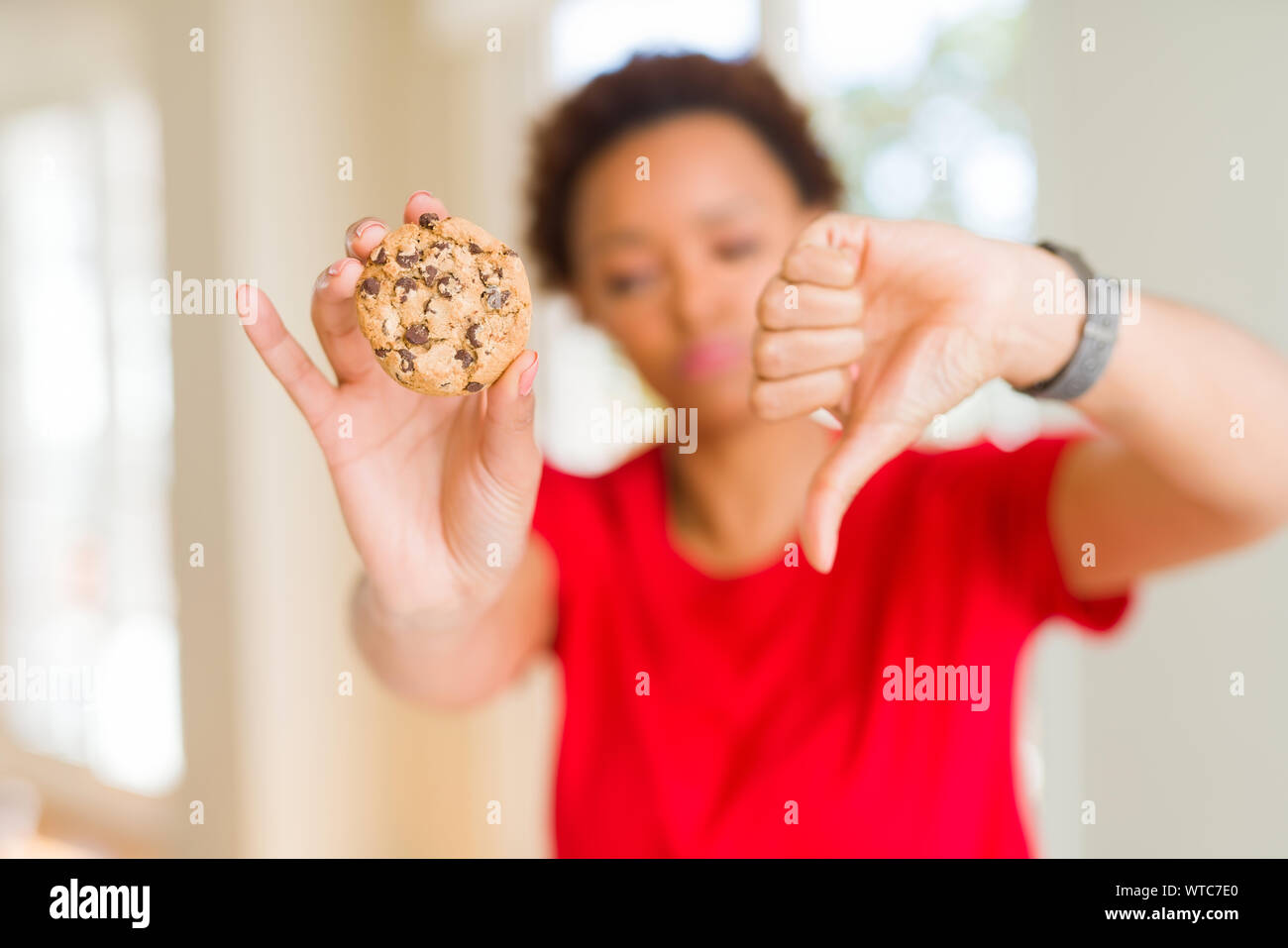 Young african american woman eating chocolate chips cookies with angry ...