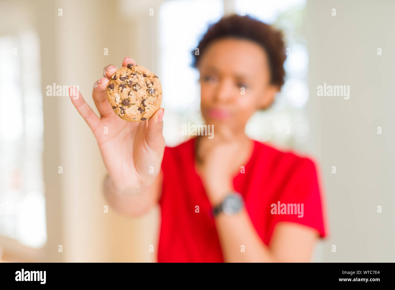 Young african american woman eating chocolate chips cookies serious ...