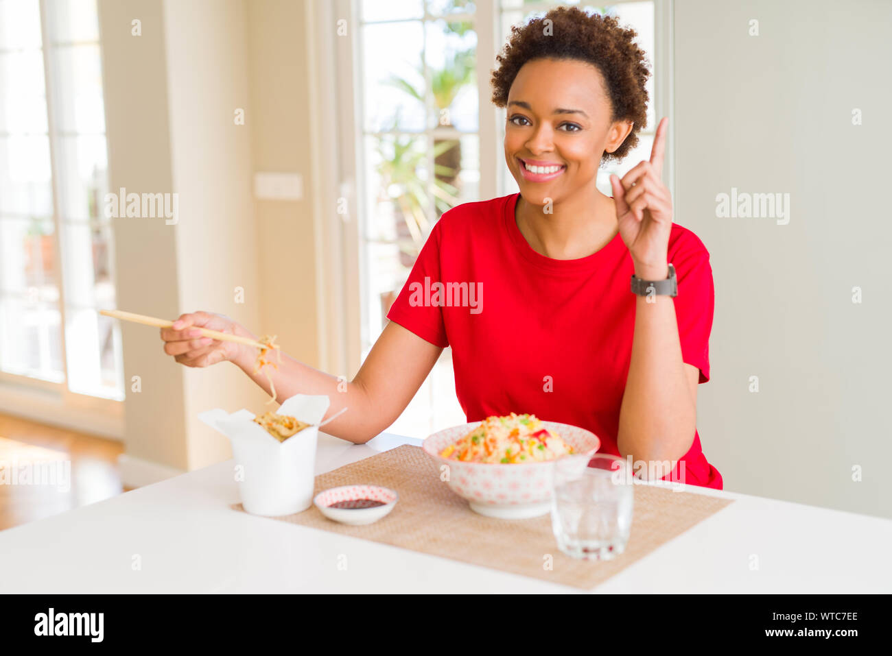 Young african american woman with afro hair eating asian food at home ...