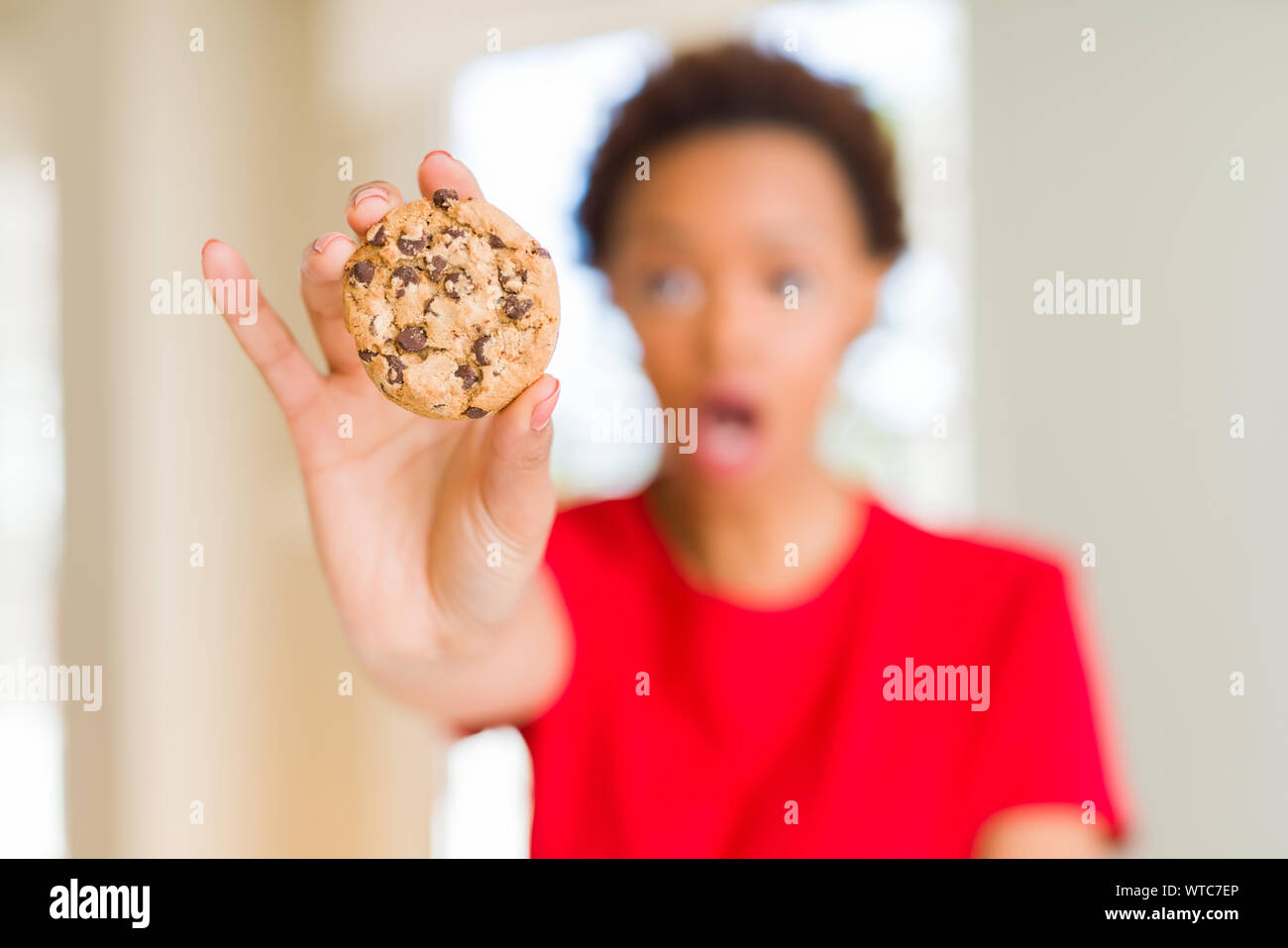 Young african american woman eating chocolate chips cookies scared in ...