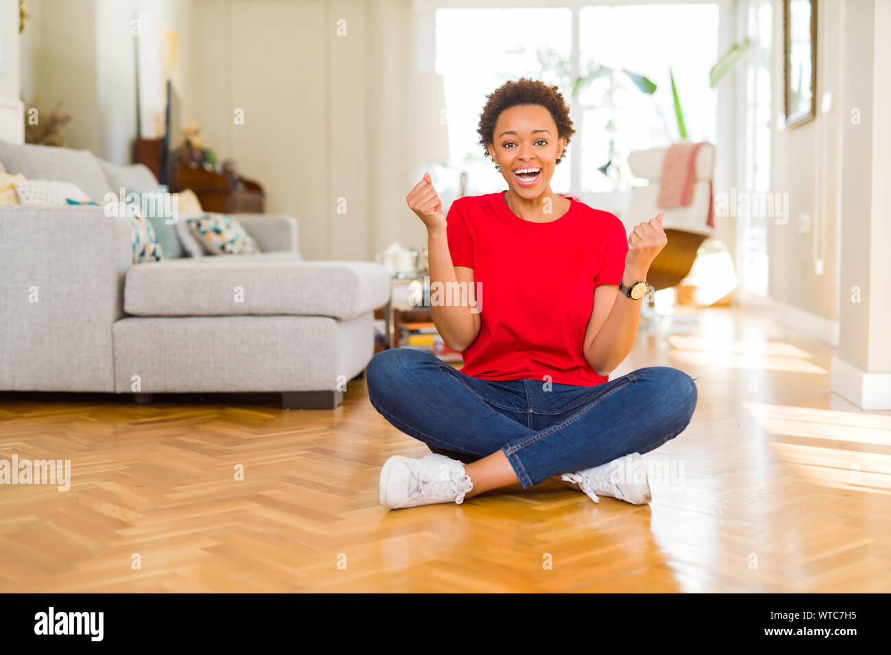 Young beautiful african american woman sitting on the floor at home ...
