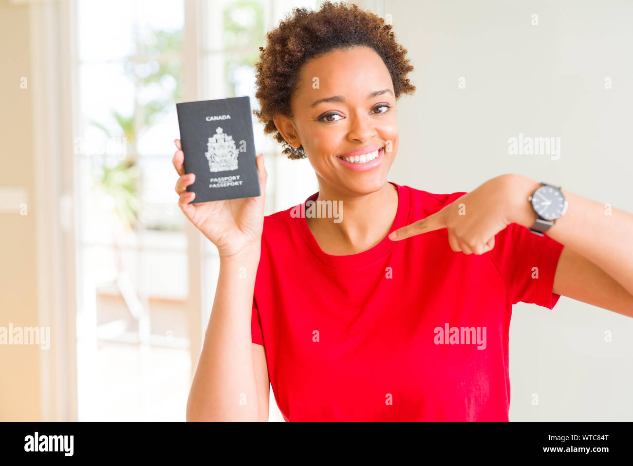 Young african american woman holding Canadian passport with surprise ...