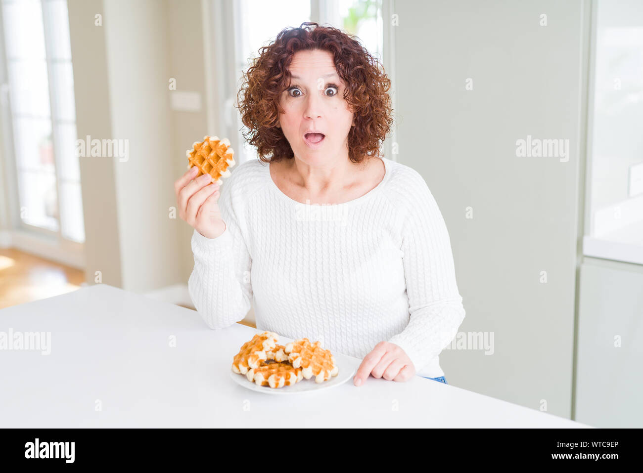 Senior woman eating sweet belgian waffle scared in shock with a ...