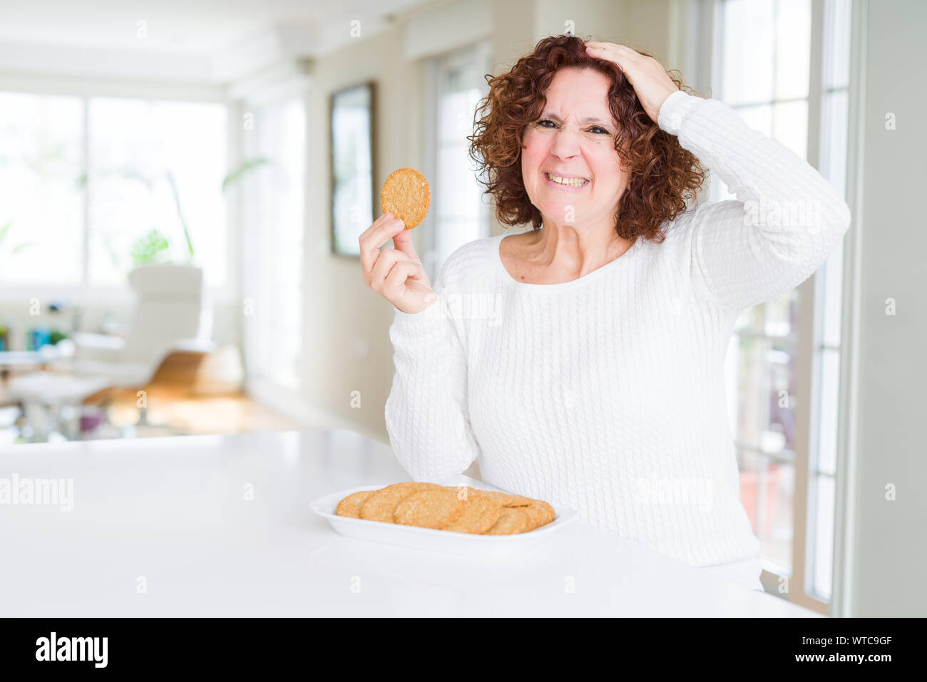 Senior woman eating healthy whole grain biscuit at home stressed with ...
