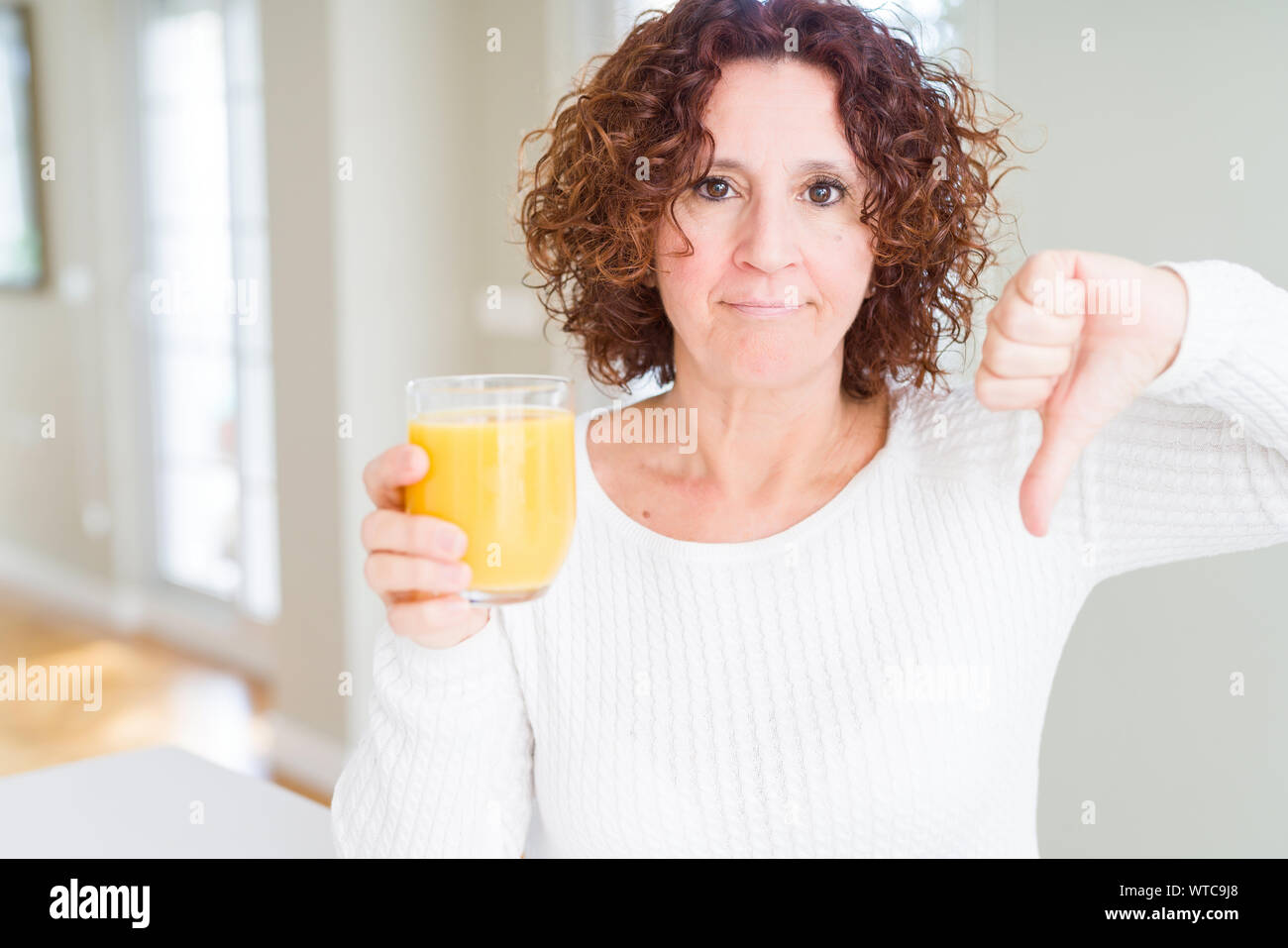 Senior woman driking a glass of fresh orange juice with angry face ...