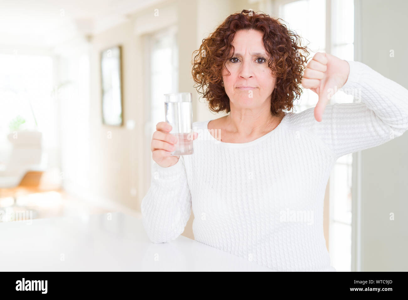 Senior woman driking a fresh glass of water with angry face, negative ...