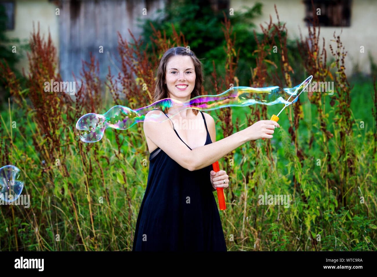 portrait of young brunette woman standing outdoors and blowing soap ...