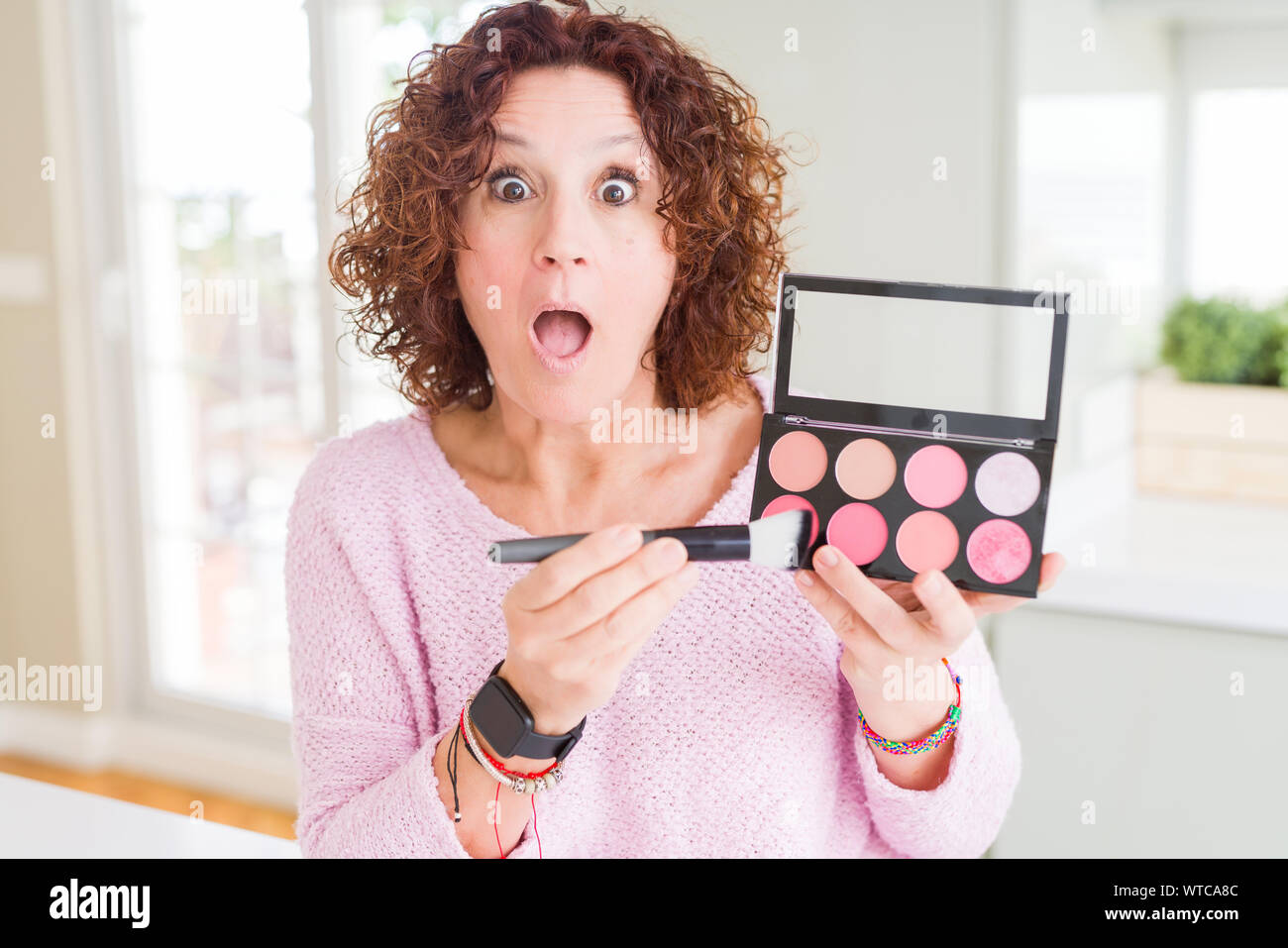 Senior woman showing palette of pink blush scared in shock with a ...