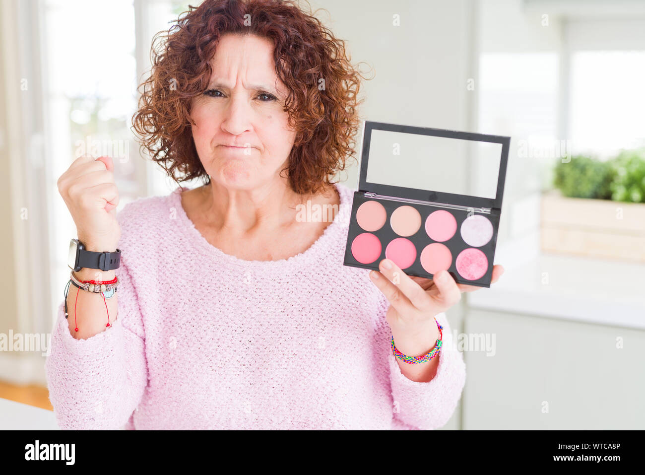 Senior woman showing palette of pink blush annoyed and frustrated ...