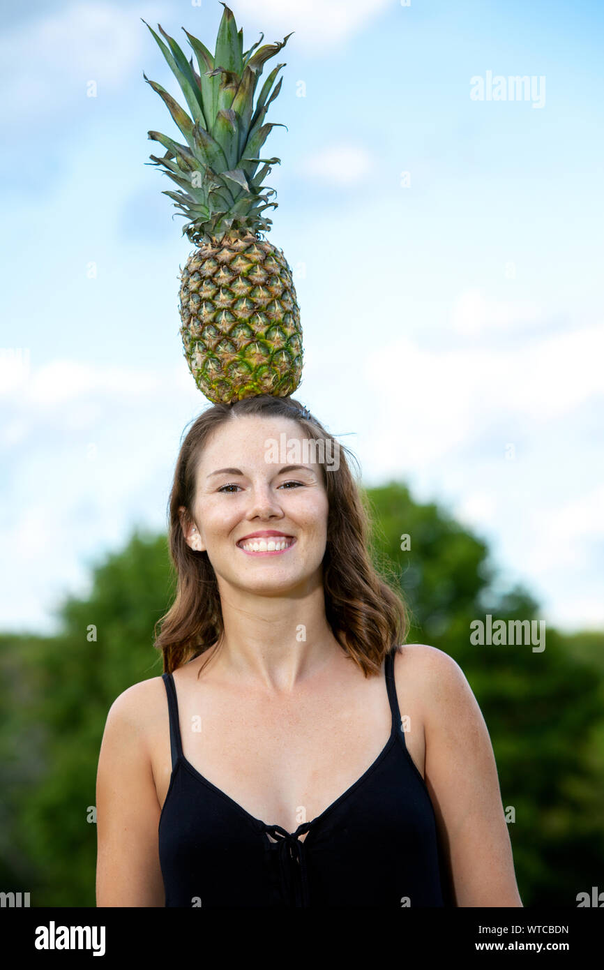 portrait of young brunette woman balancing a pineapple on her head ...