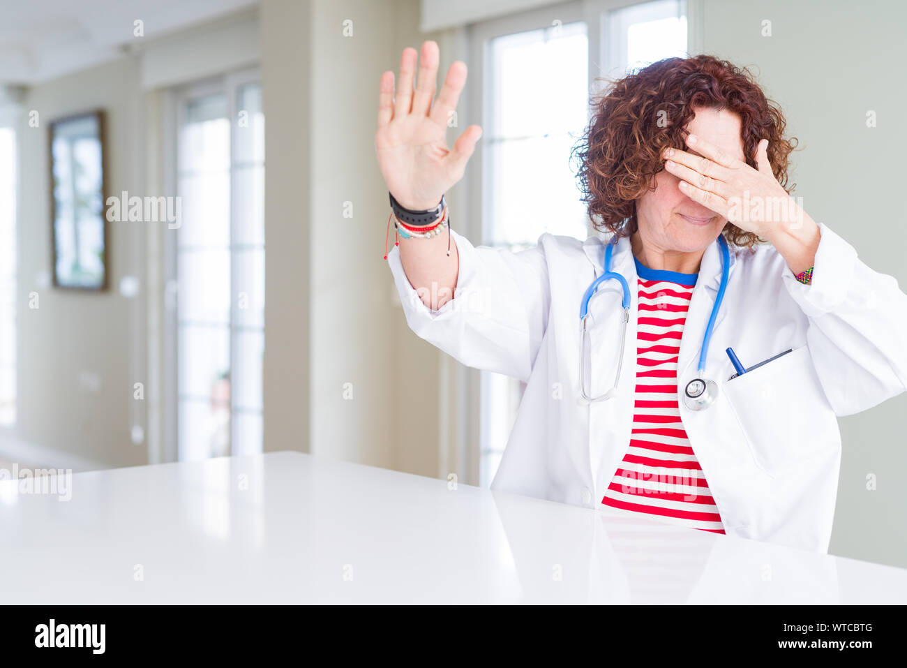Senior doctor woman wearing medical robe at the clinic covering eyes ...